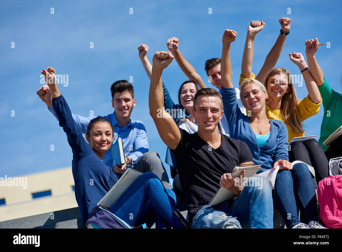 Group portrait of happy students outside in front of school sitting on ...