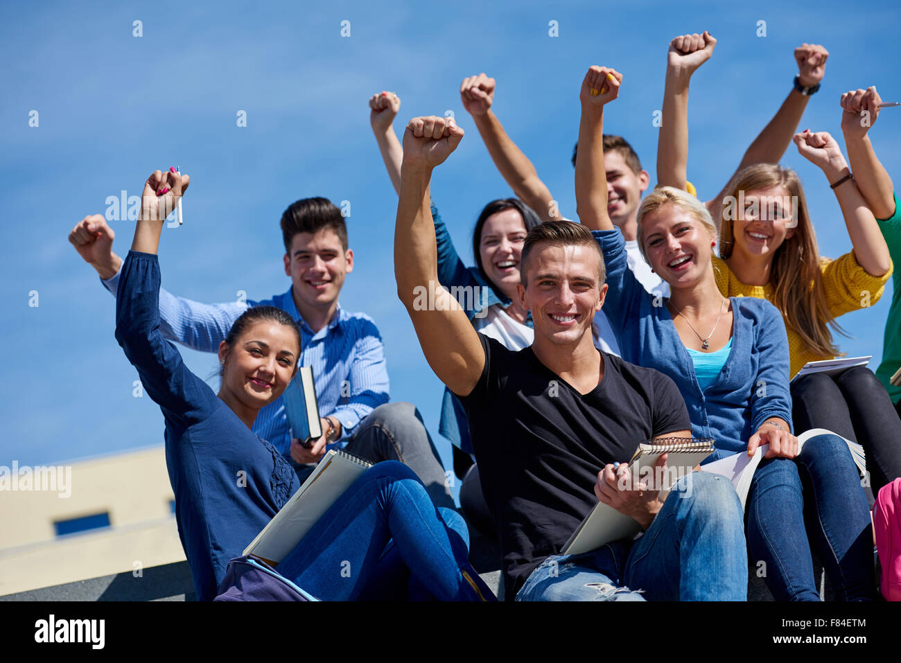 Group portrait of happy students outside in front of school sitting on ...