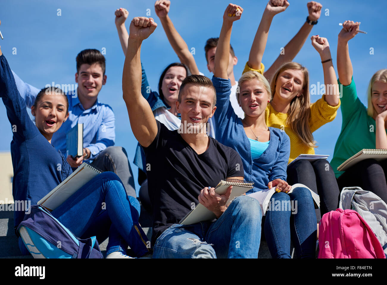 Group portrait of happy students outside in front of school sitting on ...