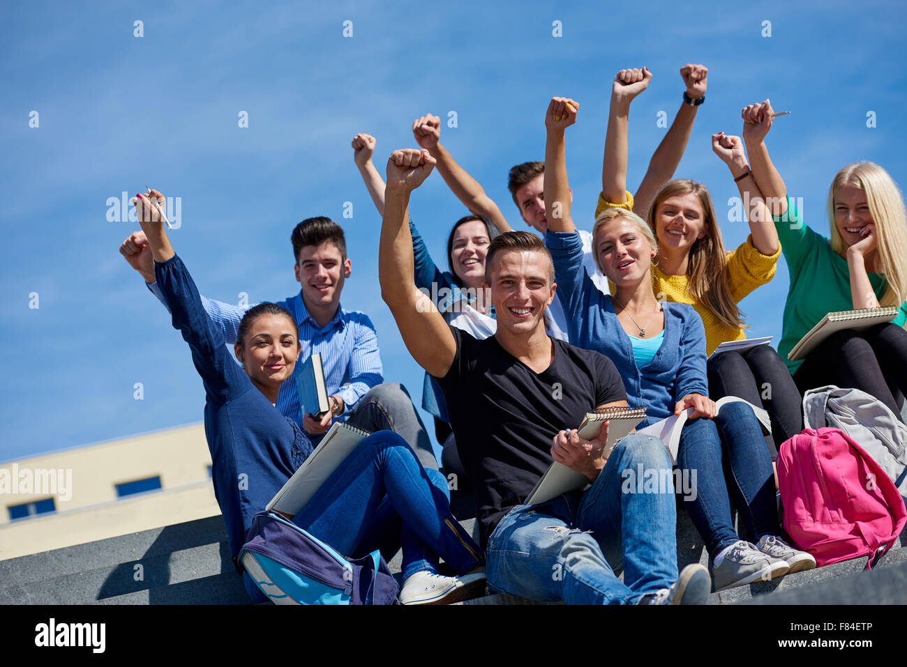Group portrait of happy students outside in front of school sitting on ...