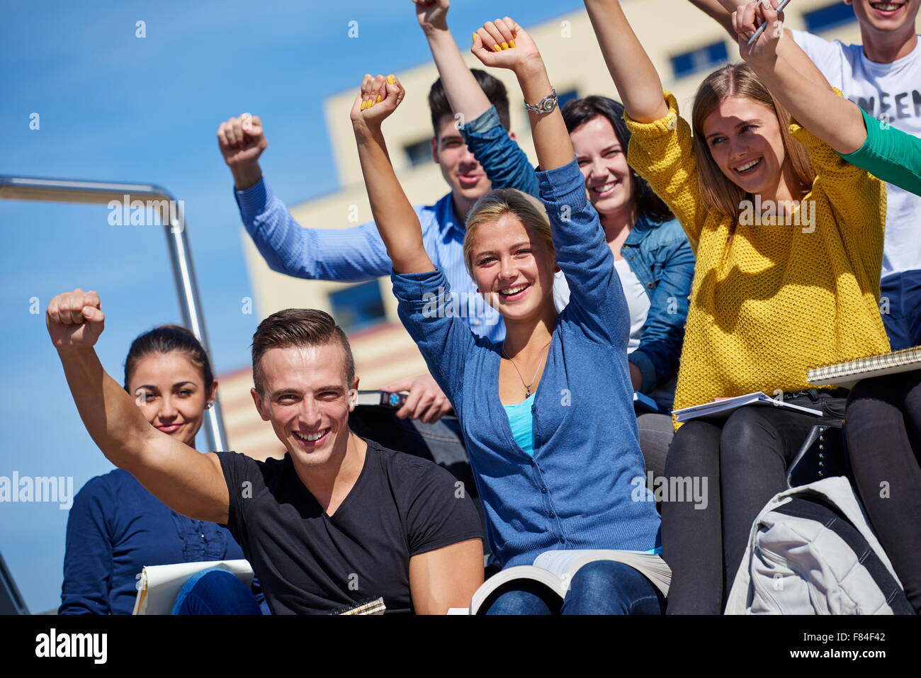 Group portrait of happy students outside in front of school sitting on ...