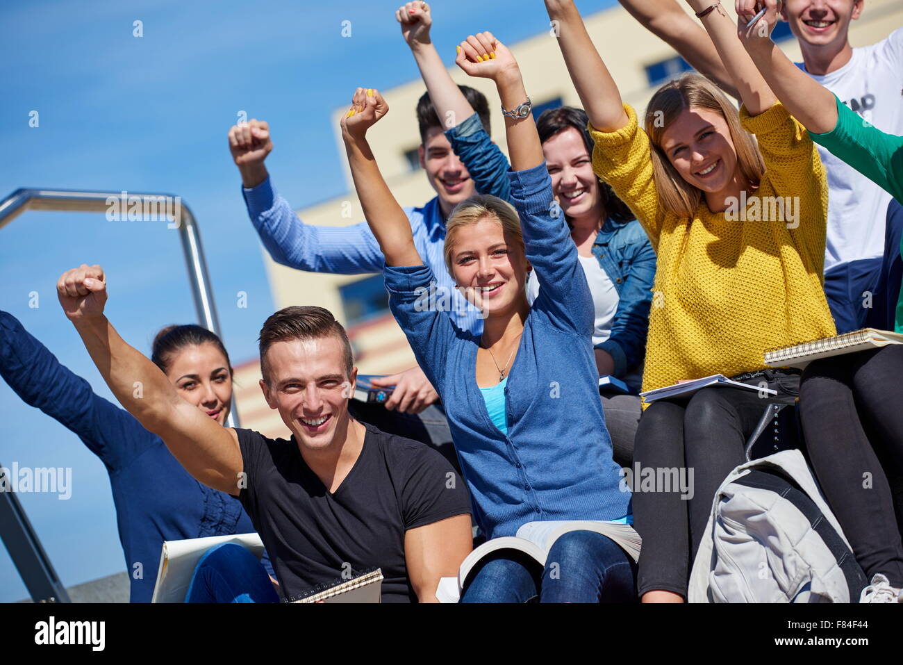 Group portrait of happy students outside in front of school sitting on ...