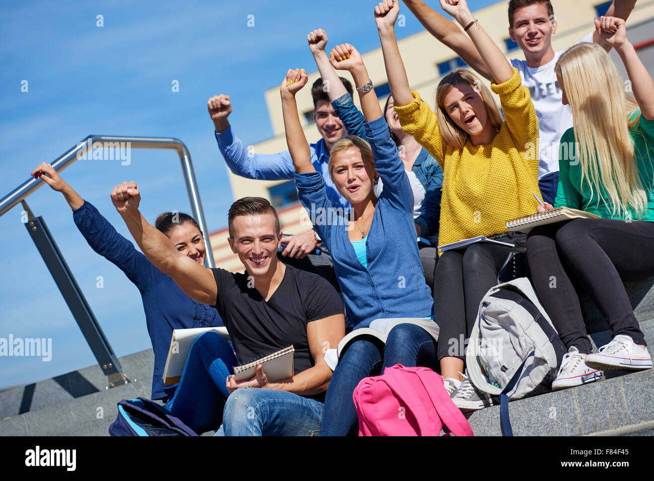 Group portrait of happy students outside in front of school sitting on ...