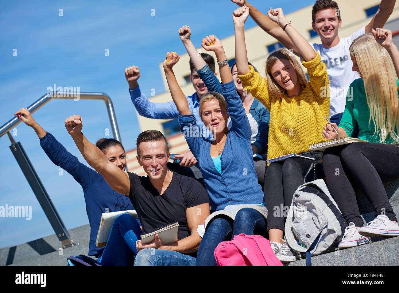 Group portrait of happy students outside in front of school sitting on ...