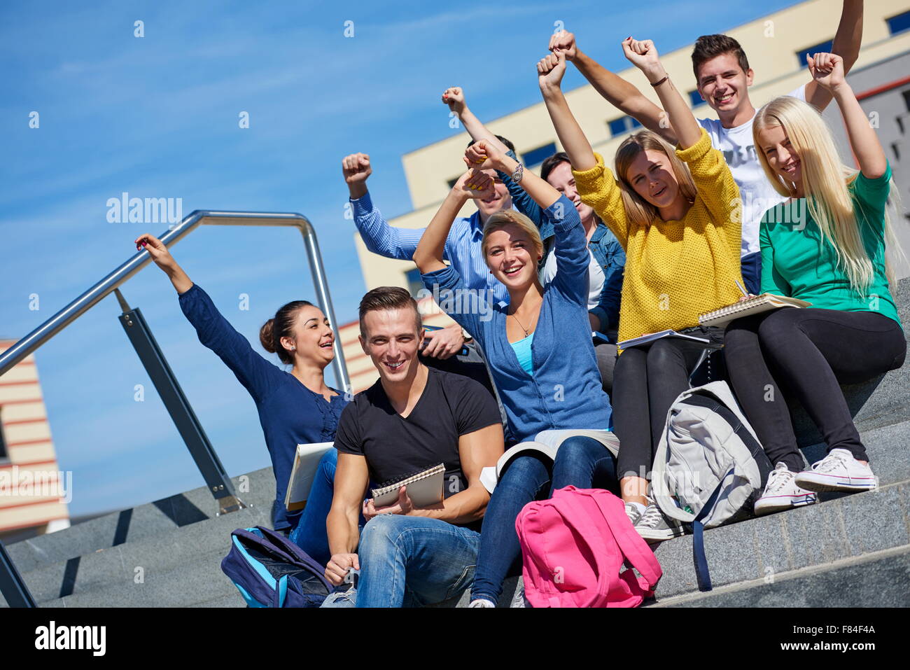 Group portrait of happy students outside in front of school sitting on ...