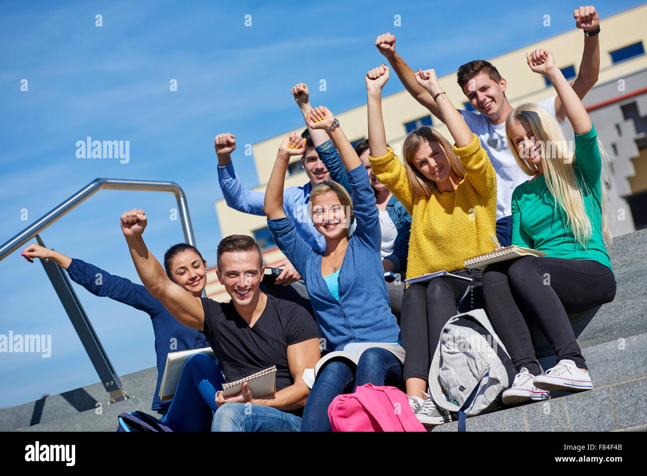 Group portrait of happy students outside in front of school sitting on ...