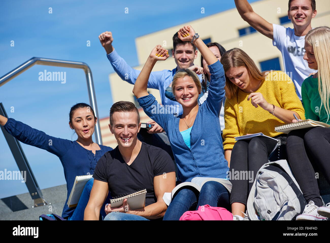Group portrait of happy students outside in front of school sitting on ...