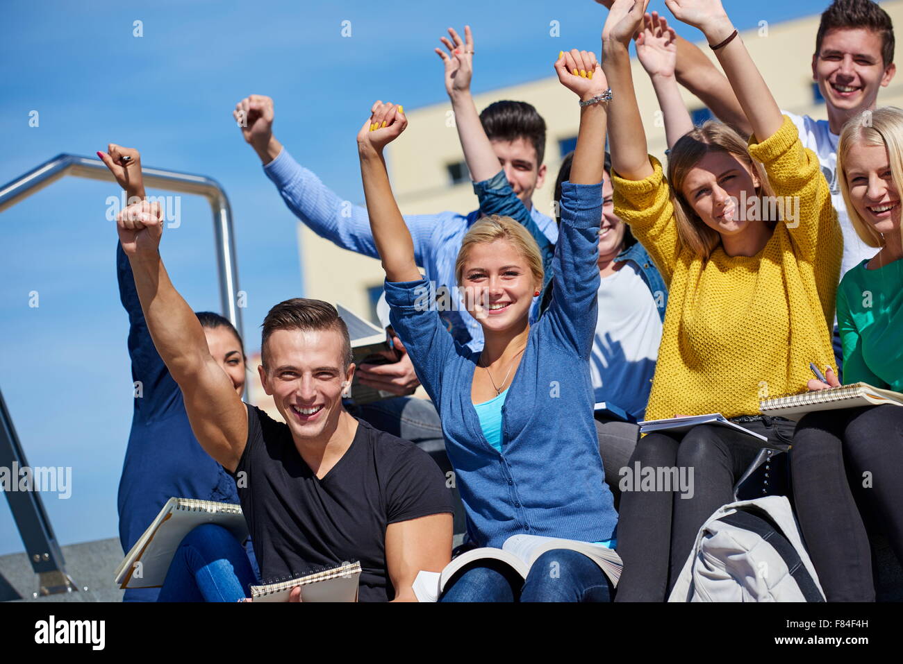 Group portrait of happy students outside in front of school sitting on ...