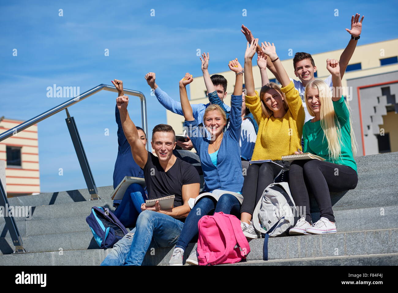 Group portrait of happy students outside in front of school sitting on ...