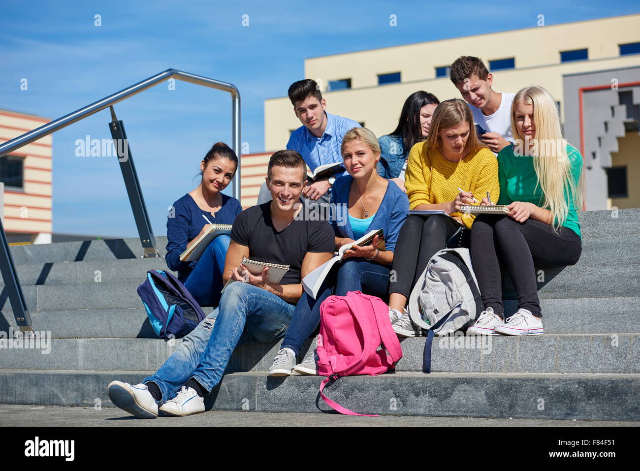 Group portrait of happy students outside in front of school sitting on ...