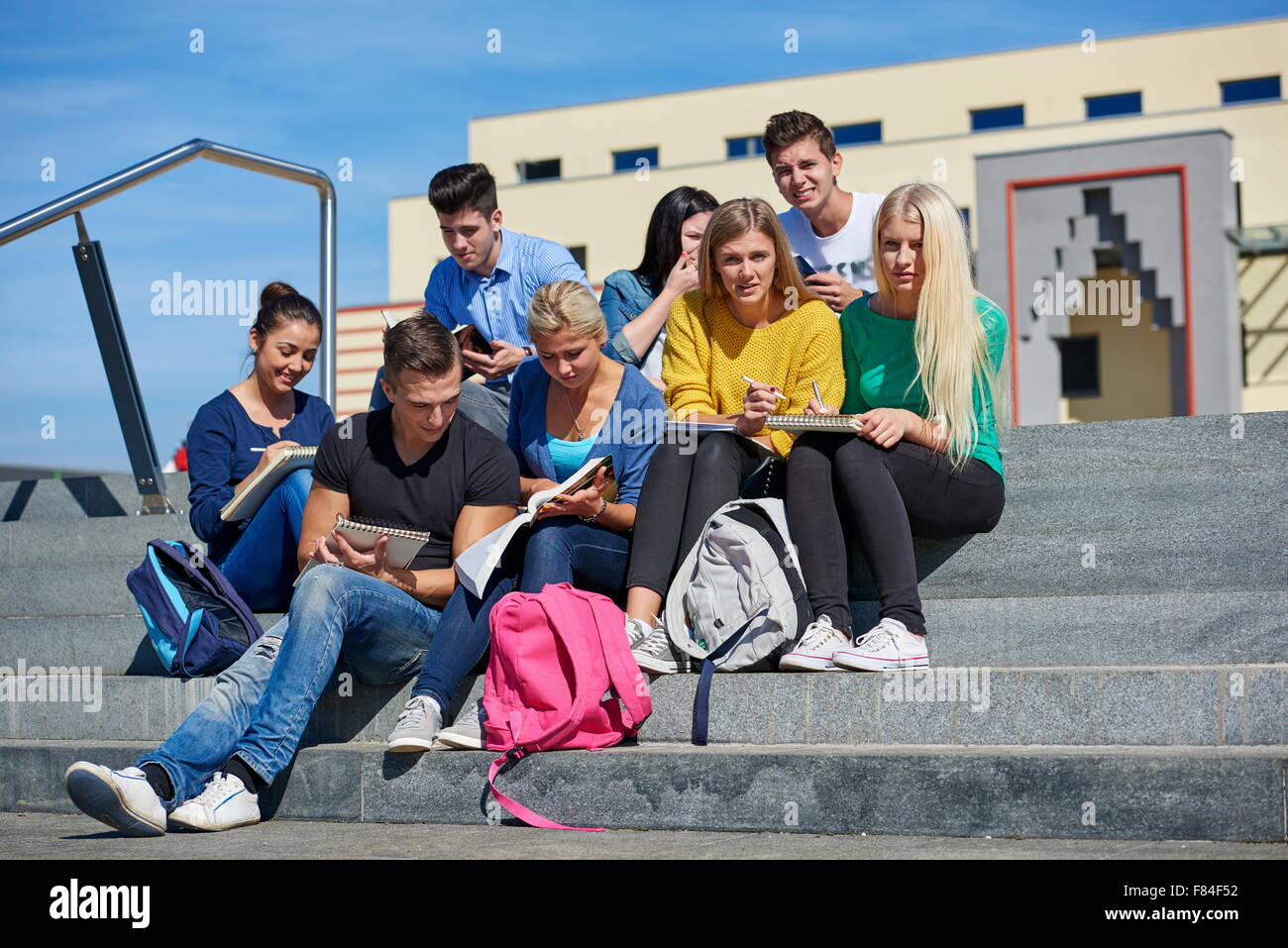 Group portrait of happy students outside in front of school sitting on ...