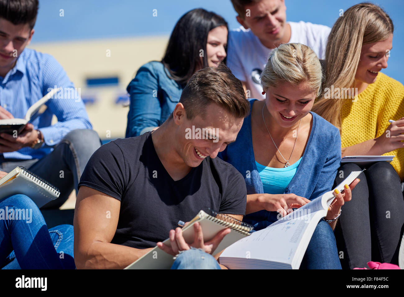 Group portrait of happy students outside in front of school sitting on ...