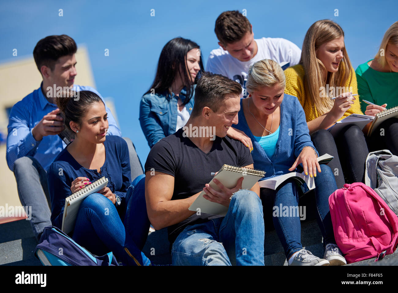 Group portrait of happy students outside in front of school sitting on ...