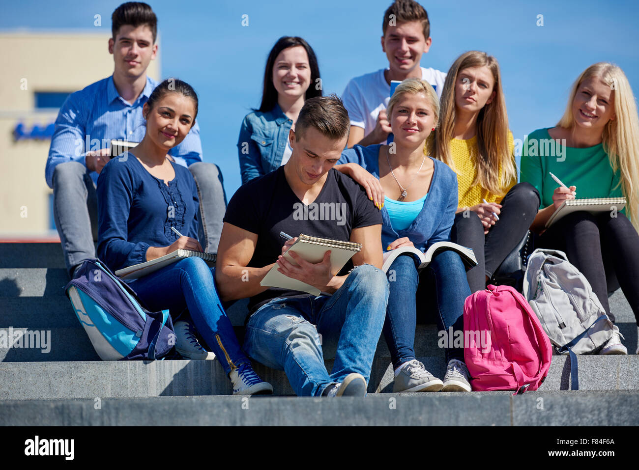 Group portrait of happy students outside in front of school sitting on ...