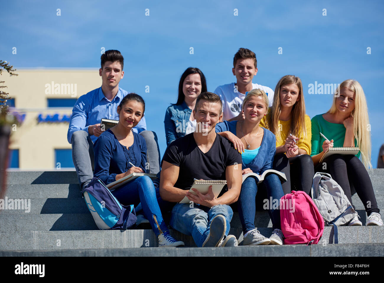 Group portrait of happy students outside in front of school sitting on ...