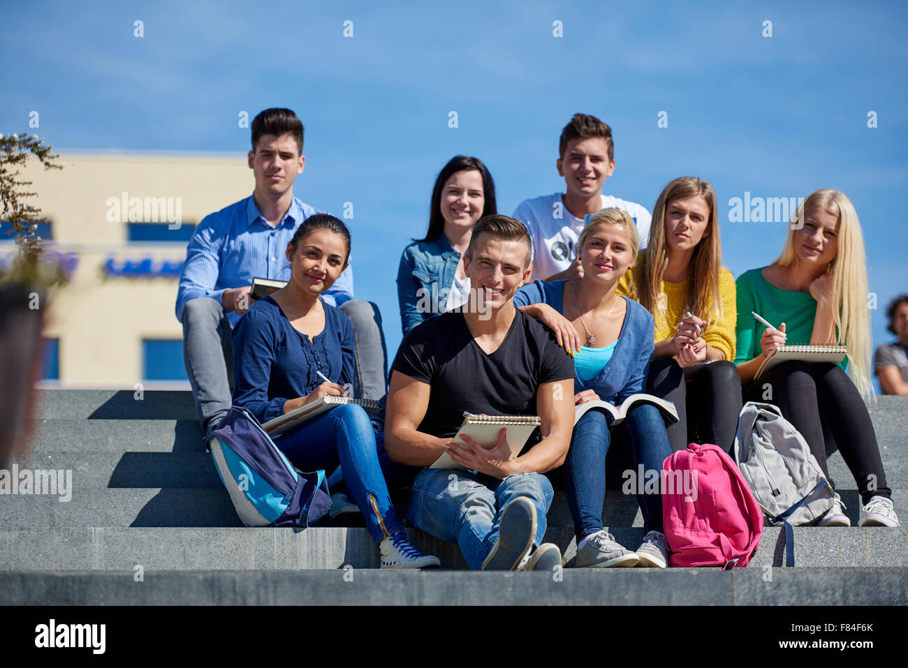 Group portrait of happy students outside in front of school sitting on ...