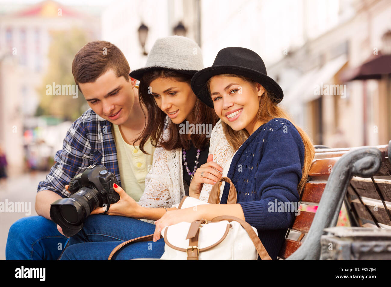 Three friends with camera sit together on bench Stock Photo - Alamy