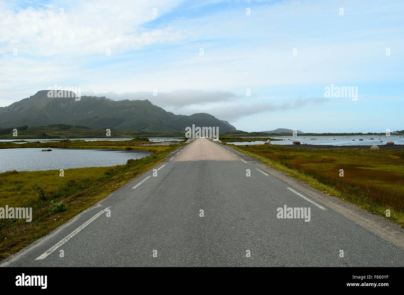 long strait road with ocean water on sides and mighty mountains in ...