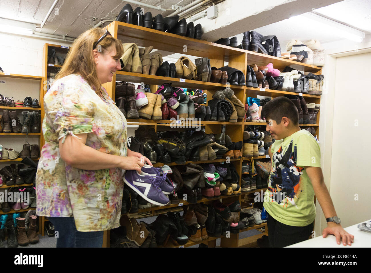 A volunteer shows donated shoes to a refugee boy. Shelves with donated ...