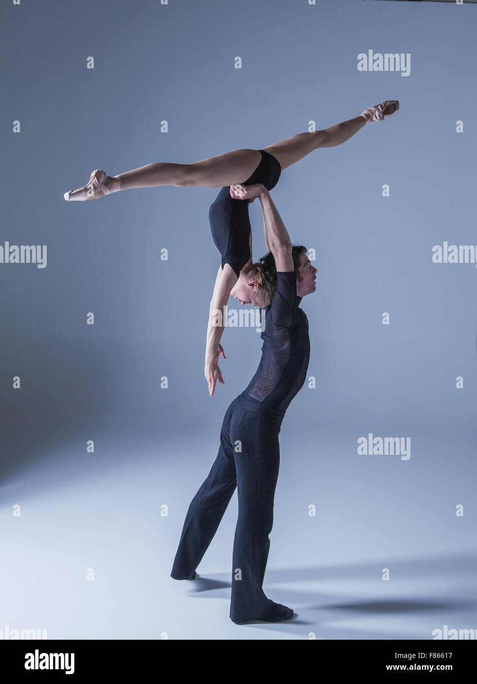 The two young modern ballet dancers in black suits posing over blue ...