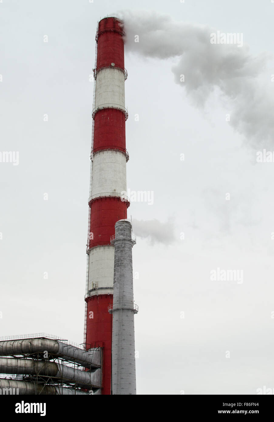 Two chimney stacks emit smoke and pollution into the white sky of an ...