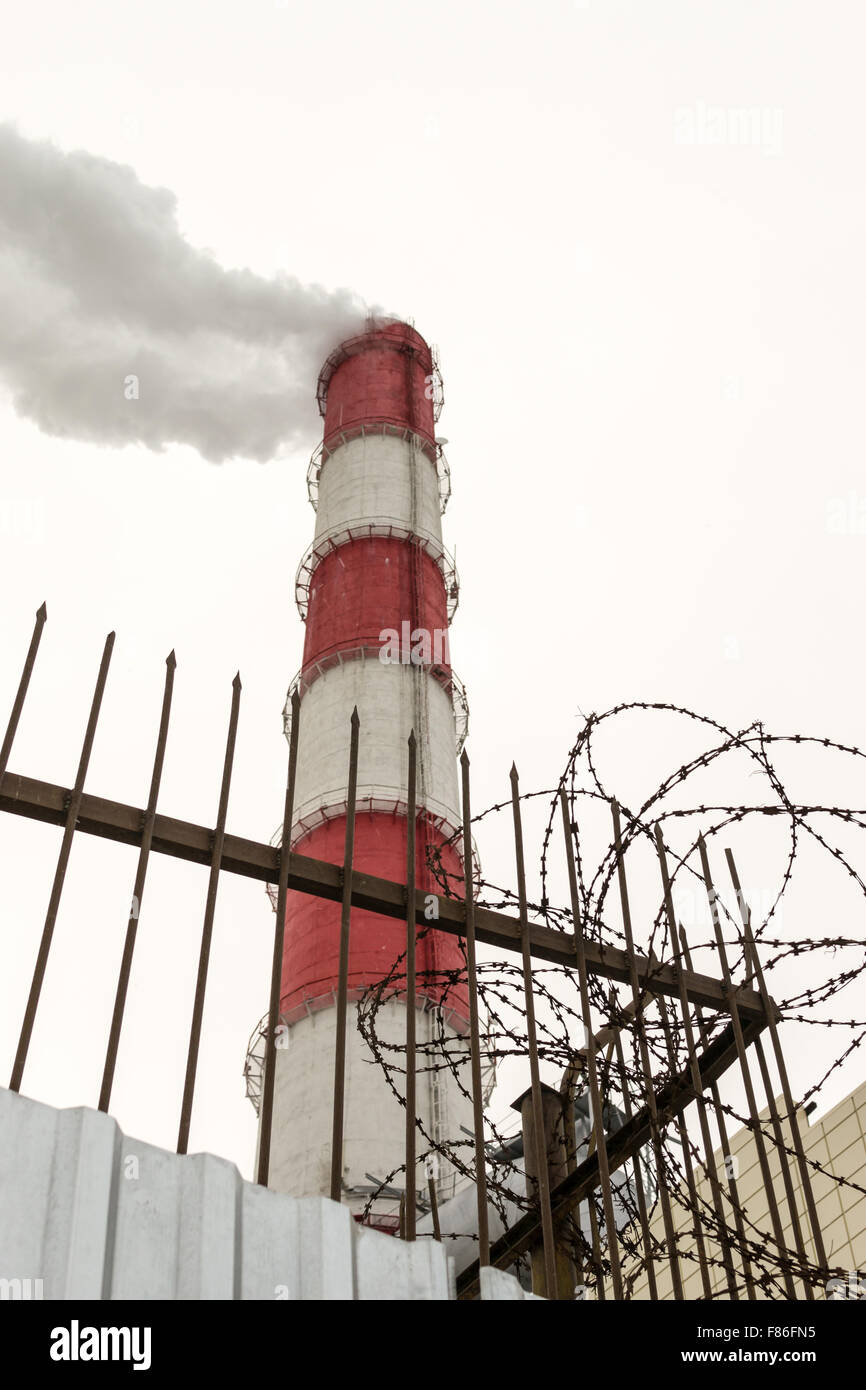 Red and white colored tall industrial chimney protected by barbed wire ...