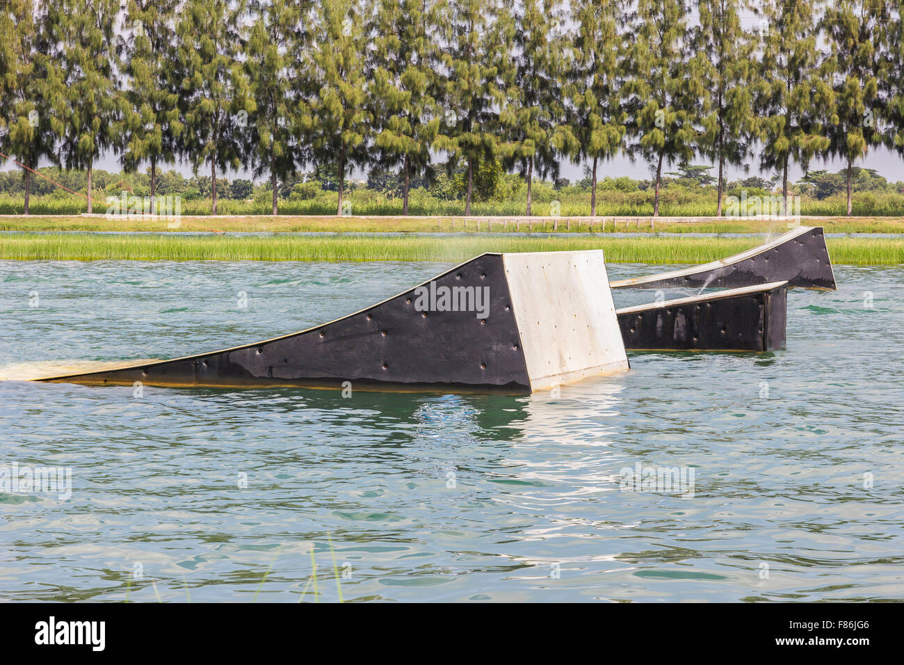 A wakeskater slides across a huge floating rail obstacle behind a boat ...
