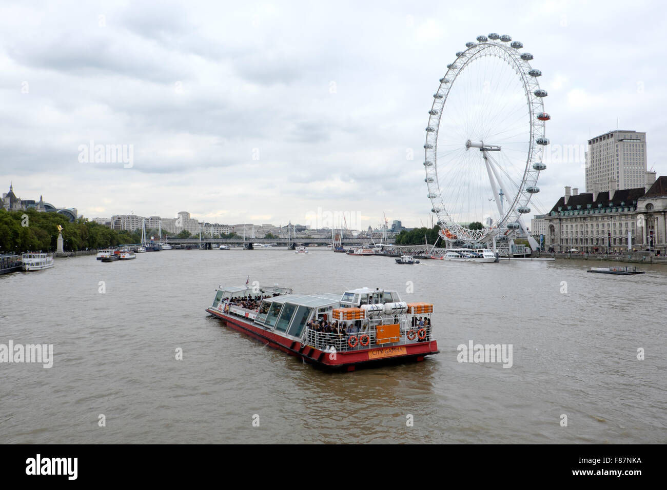 A sightseeing tour boat floats down the Thames River, passing the ...