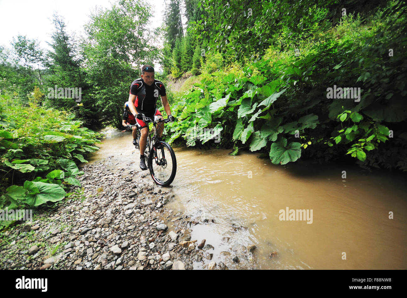 young man drive mountain bike over water river Stock Photo - Alamy