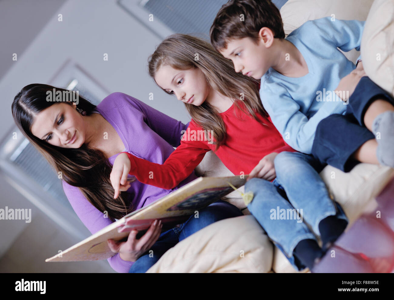 young mother read book to their kids at modern new home living room ...