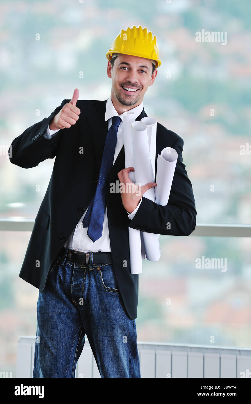 happy young architect portrait with helmet and blueprints indoor at new ...
