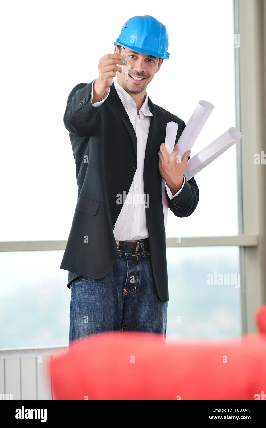 happy young architect portrait with helmet and blueprints indoor at new ...