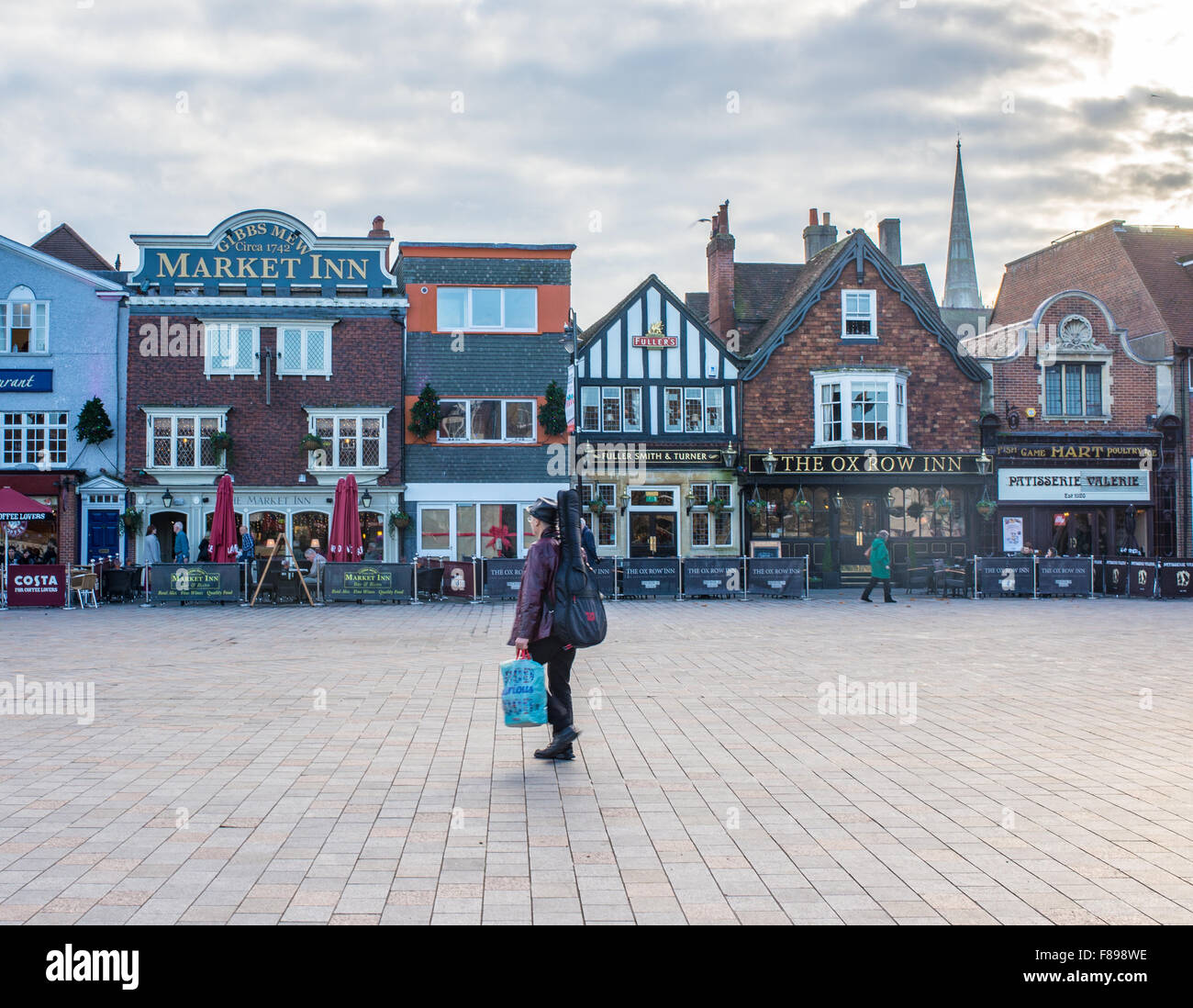 Man walking with a guitar on his back across Market Square, Salisbury ...