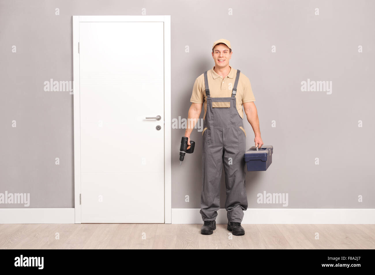 Young male locksmith holding a drill and a toolbox and standing next to ...