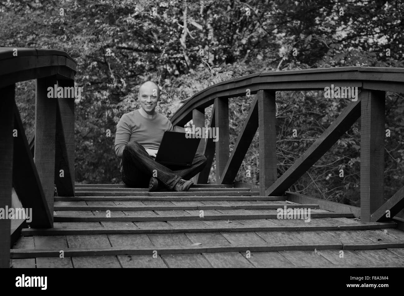 one young businessman working on laptop outdoor at wooden bridge with ...
