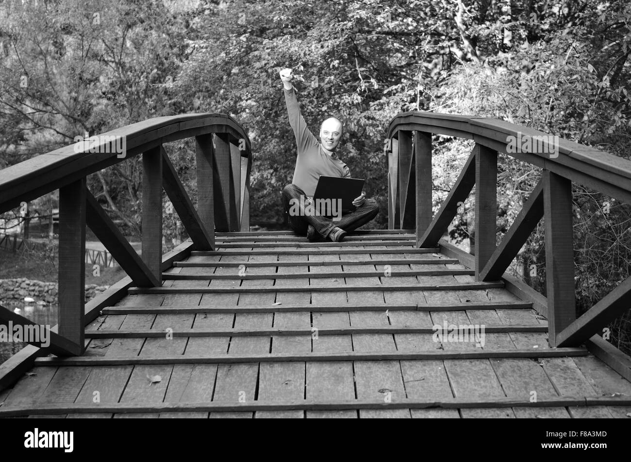one young businessman working on laptop outdoor at wooden bridge with ...
