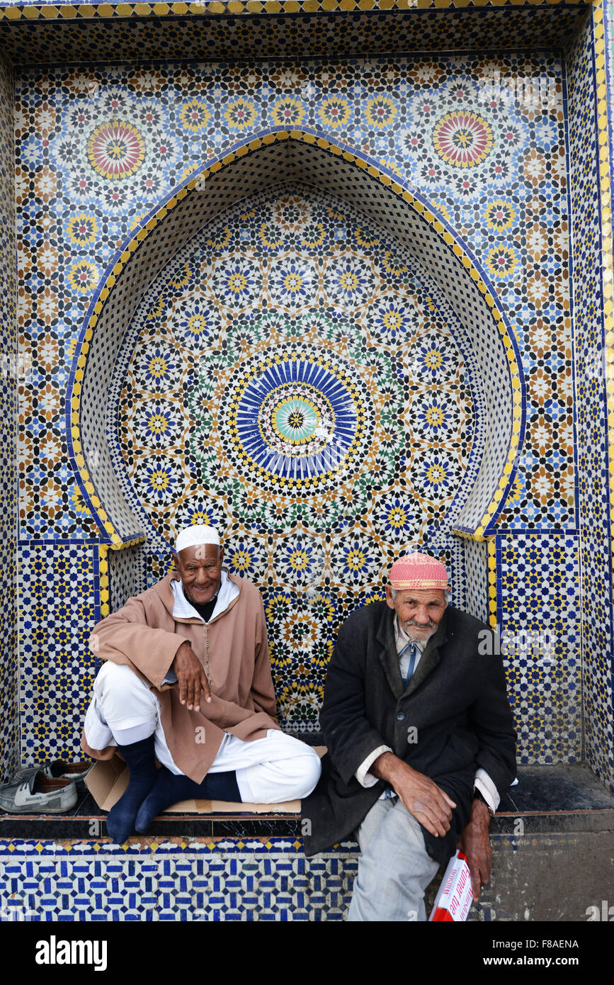 Moroccan men resting by a small colorful zellige fountain in Meknes ...