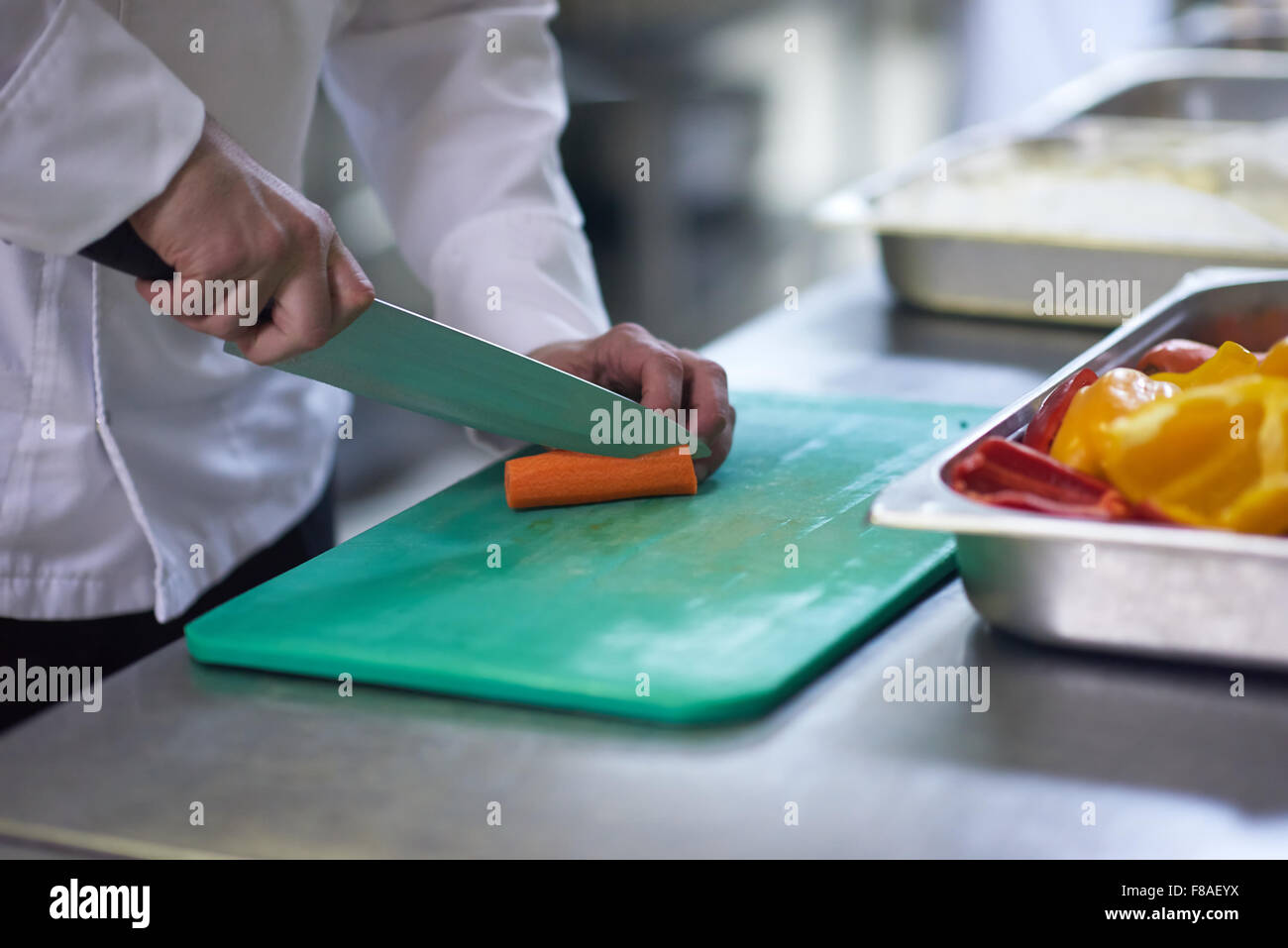 chef in hotel kitchen slice vegetables with knife and prepare food ...