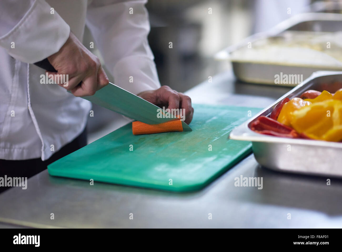 chef in hotel kitchen slice vegetables with knife and prepare food ...