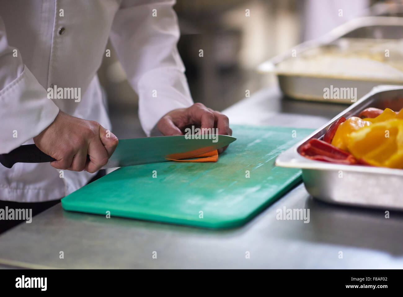 chef in hotel kitchen slice vegetables with knife and prepare food ...
