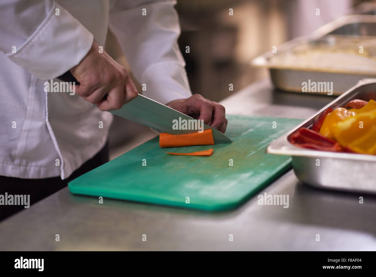 chef in hotel kitchen slice vegetables with knife and prepare food ...