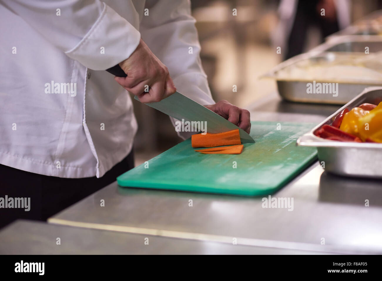 chef in hotel kitchen slice vegetables with knife and prepare food ...