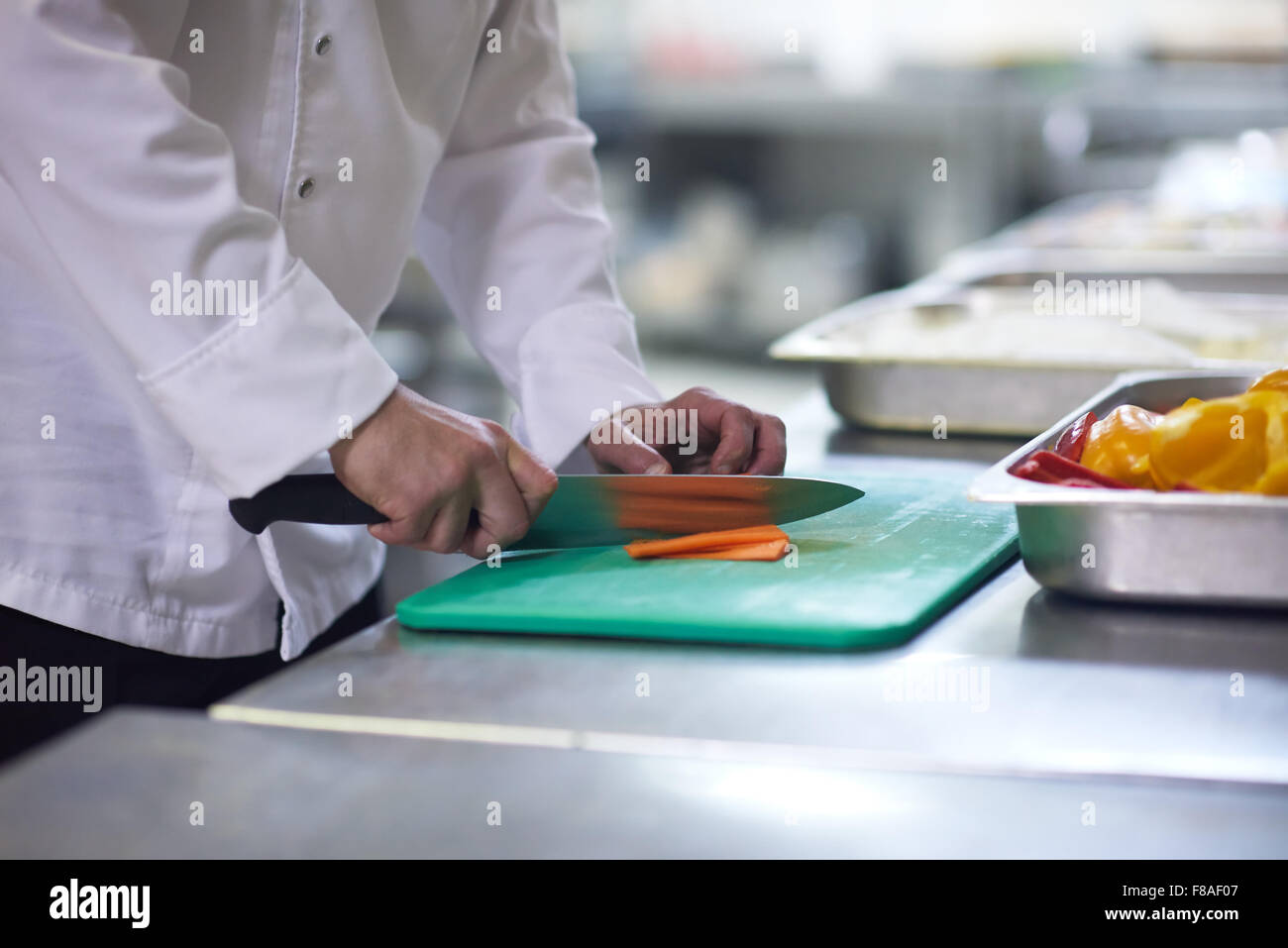chef in hotel kitchen slice vegetables with knife and prepare food ...