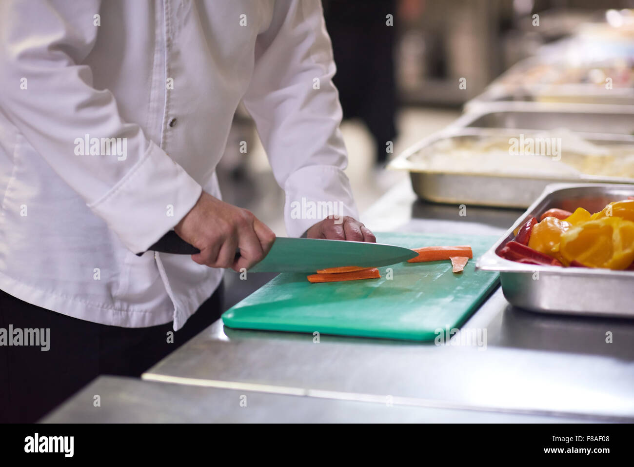 chef in hotel kitchen slice vegetables with knife and prepare food ...