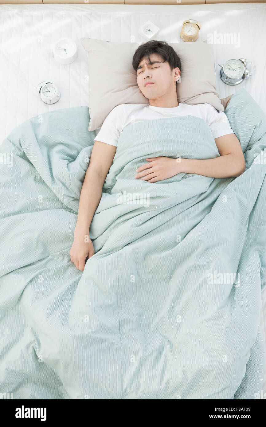 Frowned man in bed with many alarm clocks Stock Photo - Alamy