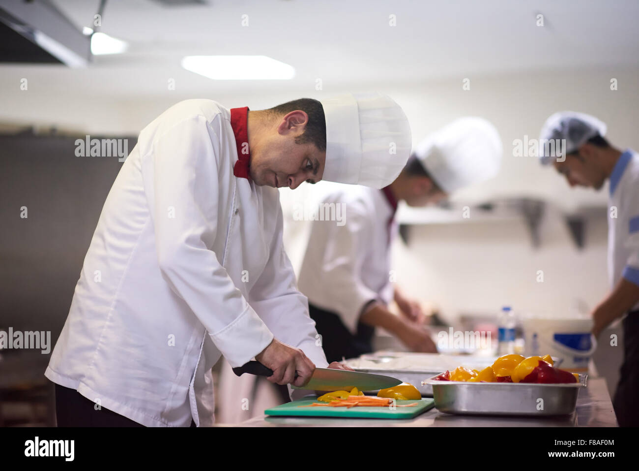 chef in hotel kitchen slice vegetables with knife and prepare food ...