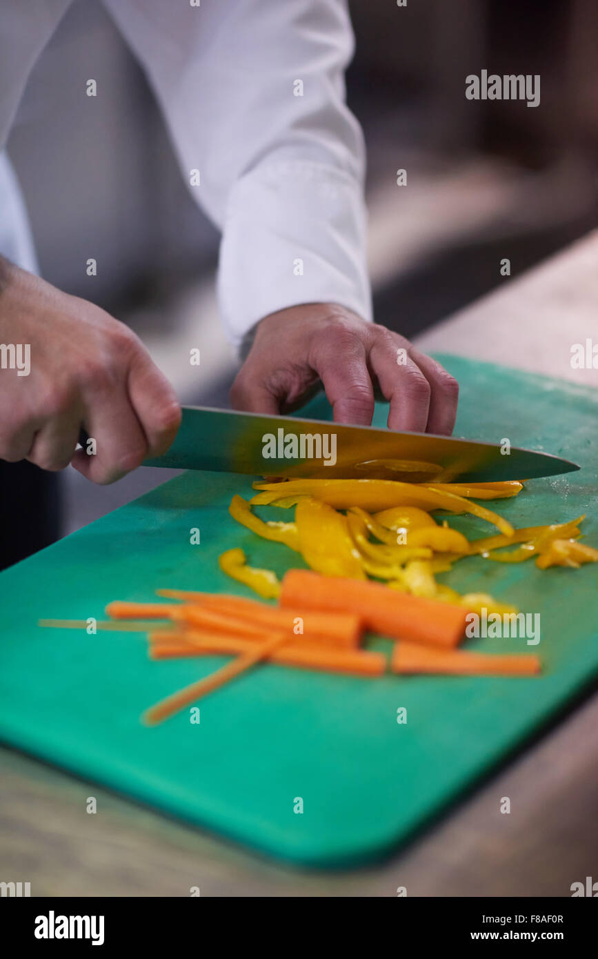 chef in hotel kitchen slice vegetables with knife and prepare food ...