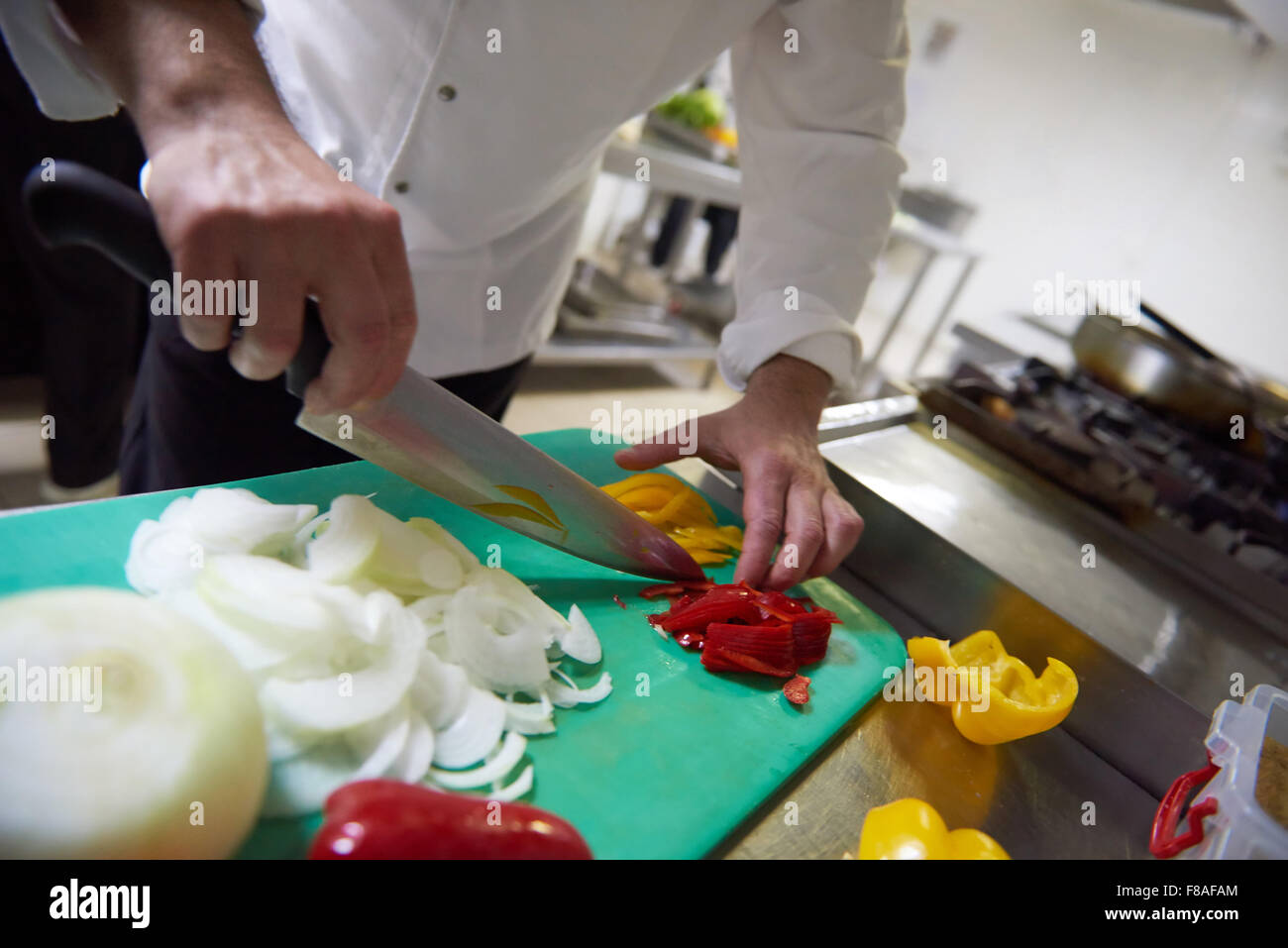 chef in hotel kitchen slice vegetables with knife and prepare food ...
