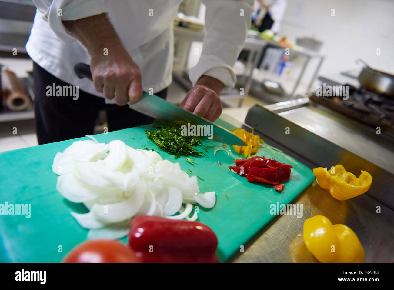 chef in hotel kitchen slice vegetables with knife and prepare food ...