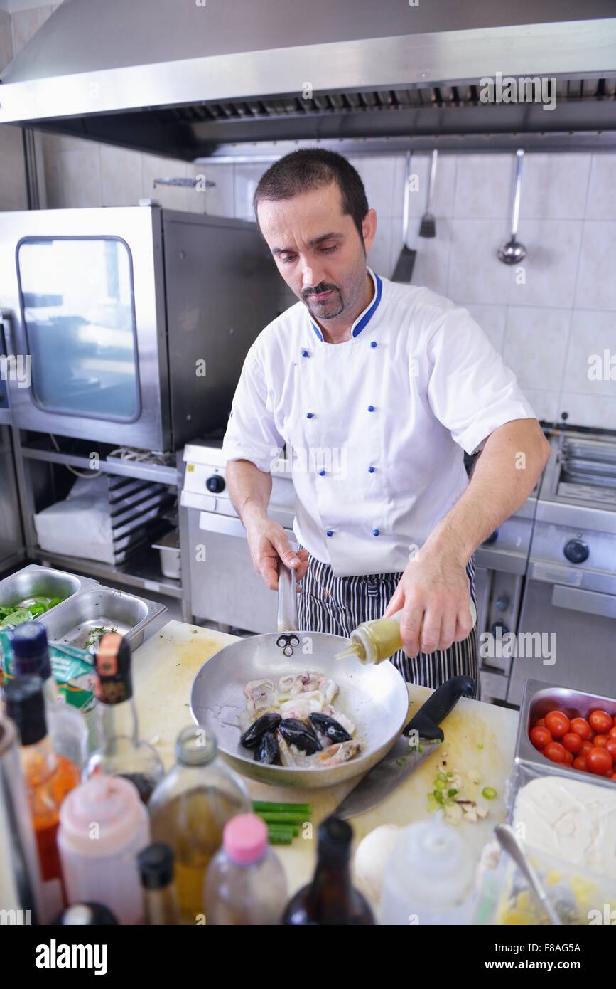 Handsome chef dressed in white uniform decorating pasta salad and ...